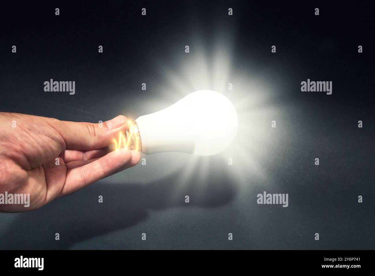 Hand holding lit light bulb. Dark background Stock Photo - Alamy
