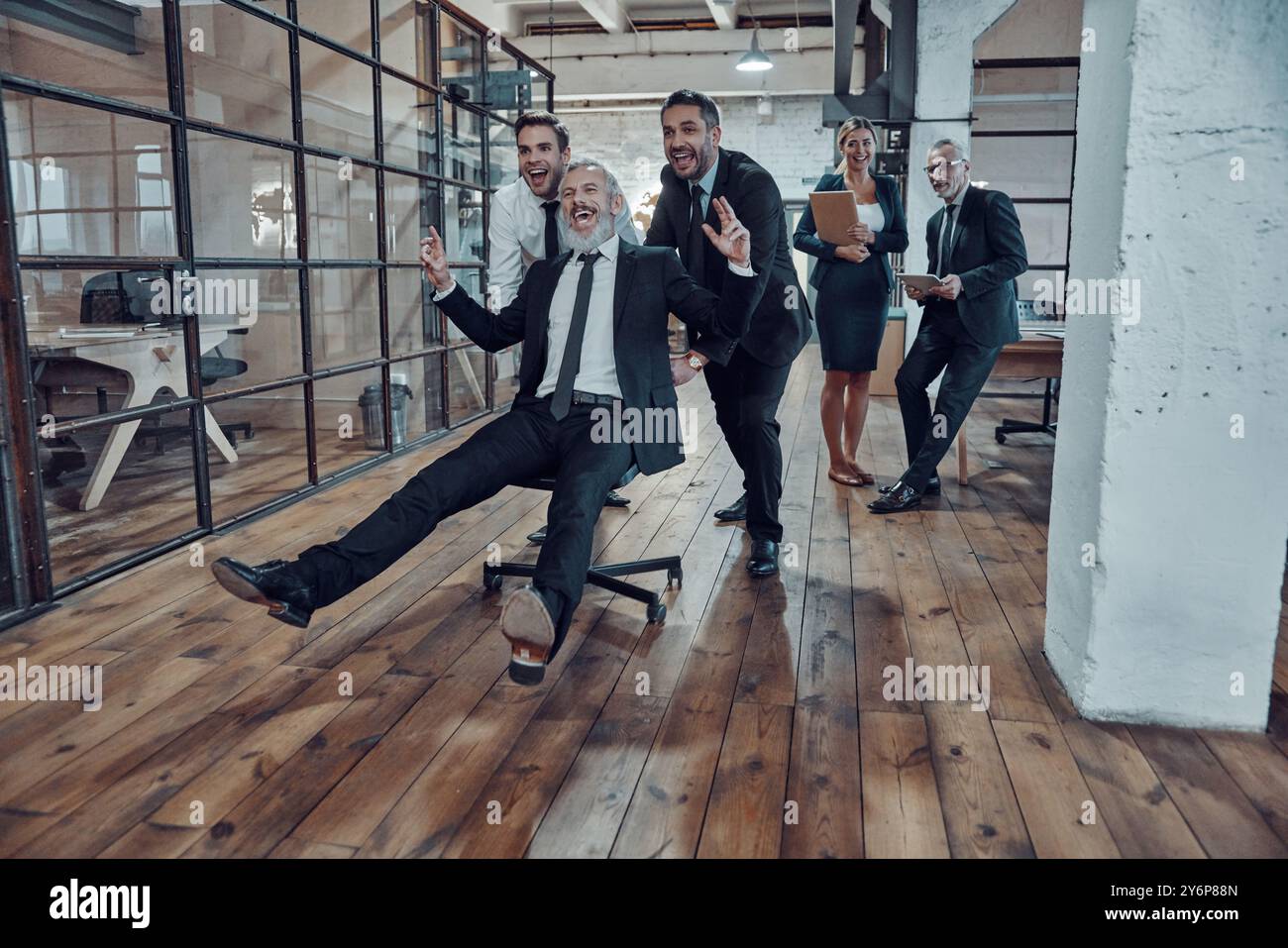 Playful businessmen pushing their boss on the office chair while ...