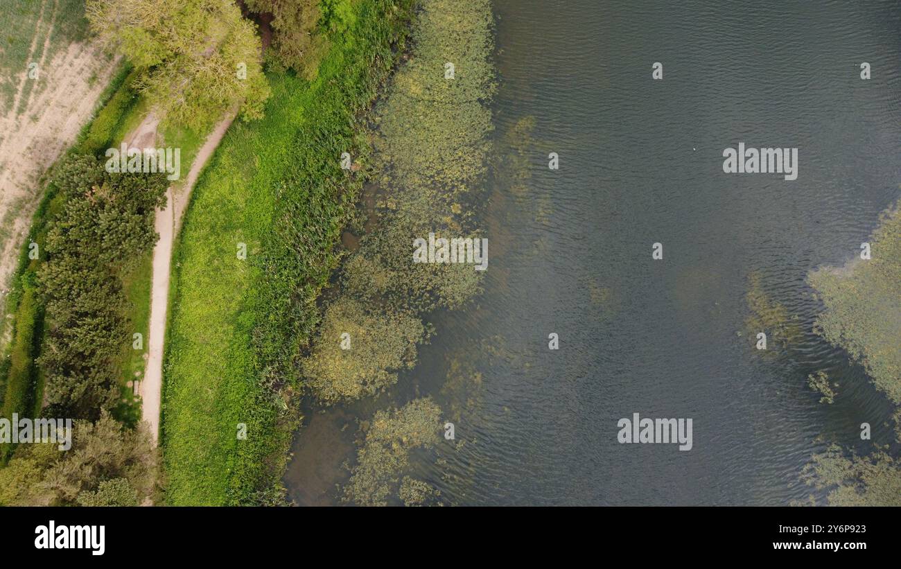 An aerial view of a lakeside path with lush greenery and serene water ...