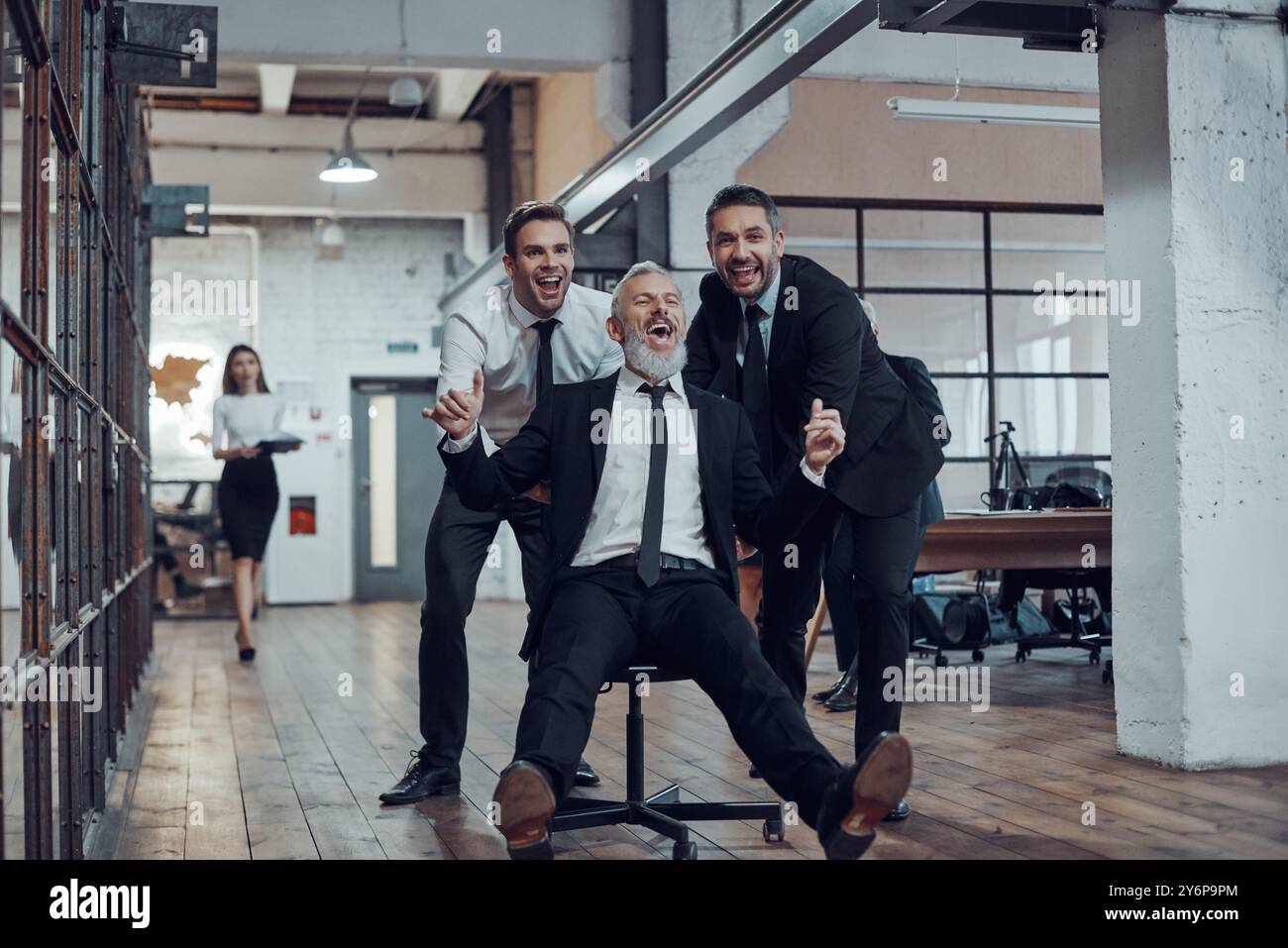 Cheerful businessmen pushing their boss on the office chair while ...