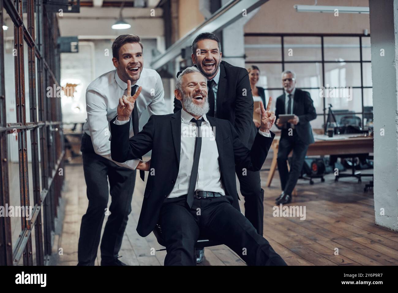Cheerful businessmen pushing their boss on the office chair while ...