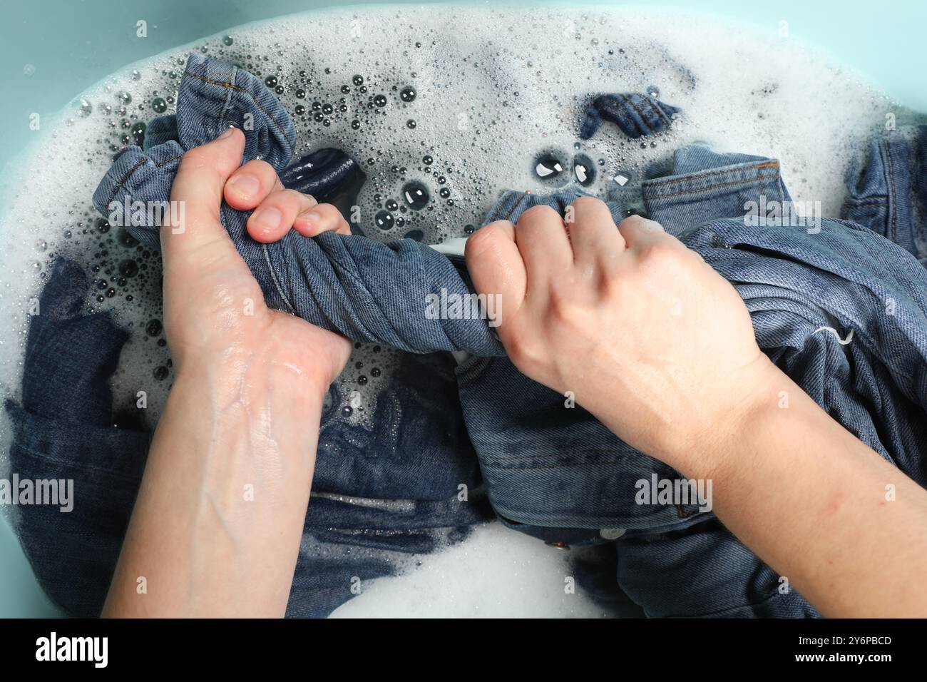 Woman washing denim clothes with soap and water in basin, top view ...