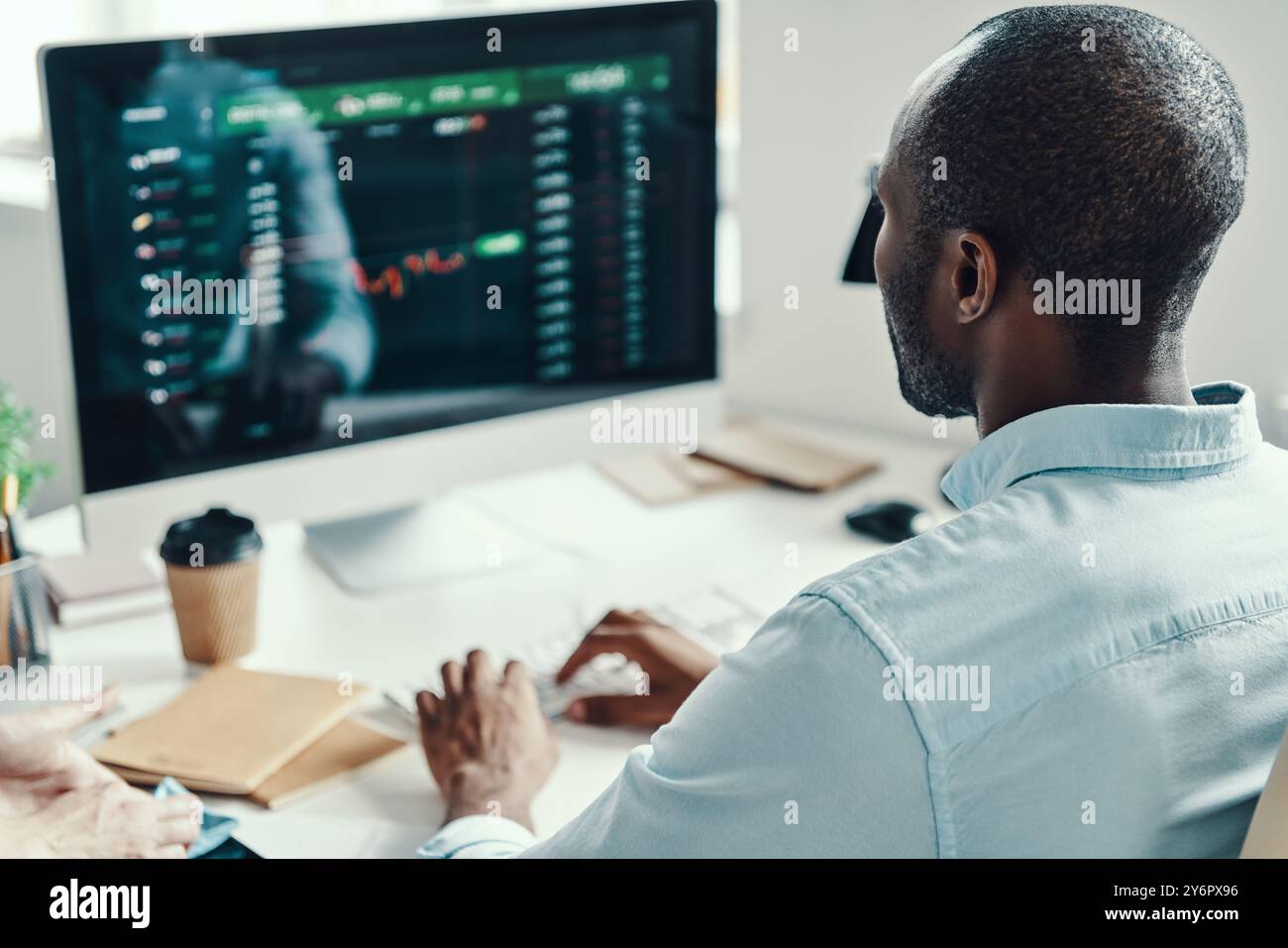 Rear view of young African man in shirt using computer while working in ...
