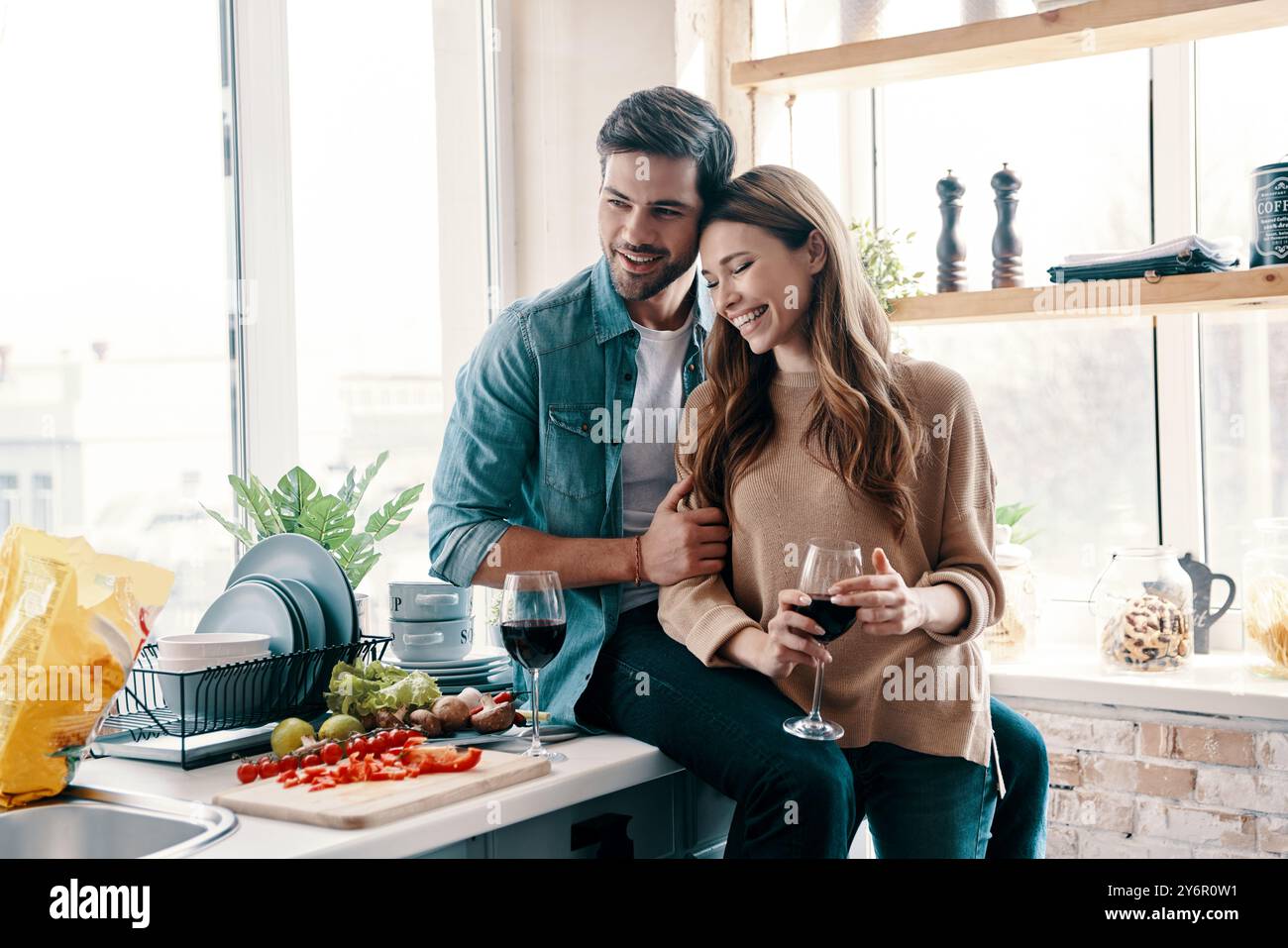 Moments of intimacy. Beautiful young couple cooking dinner and drinking ...