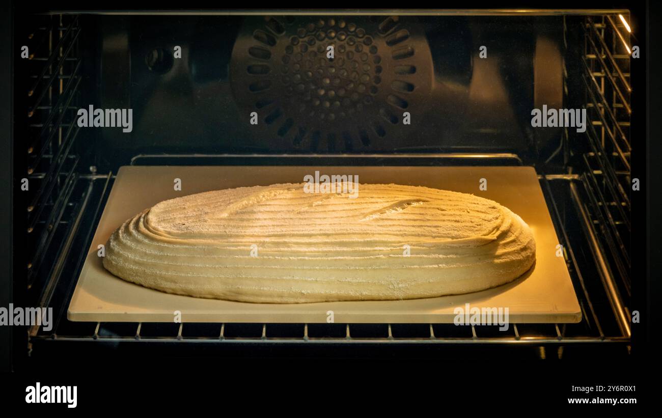 Oval-shaped bread dough on a baking stone seen through the oven door as ...