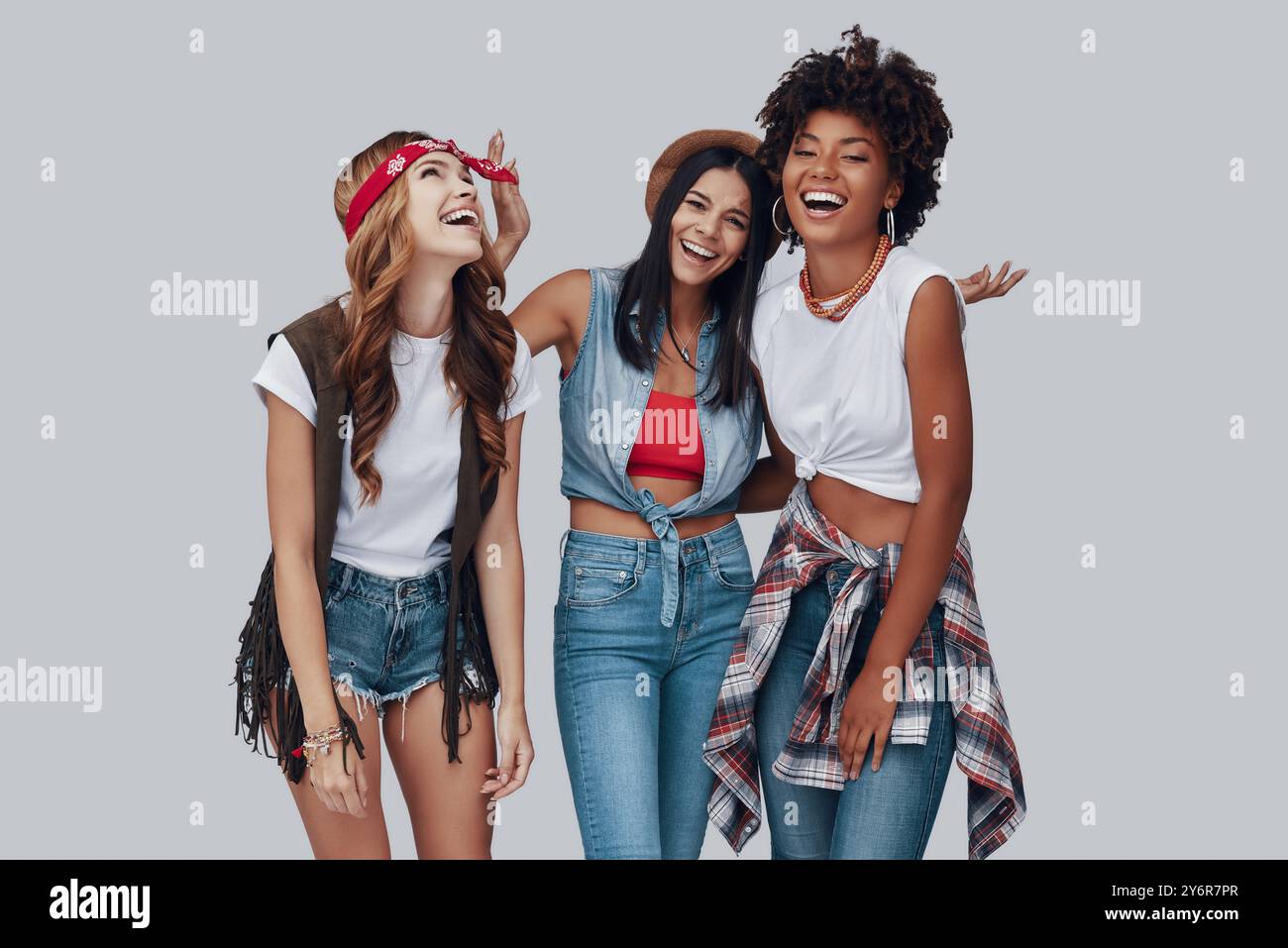 Three attractive stylish young women laughing while standing against ...