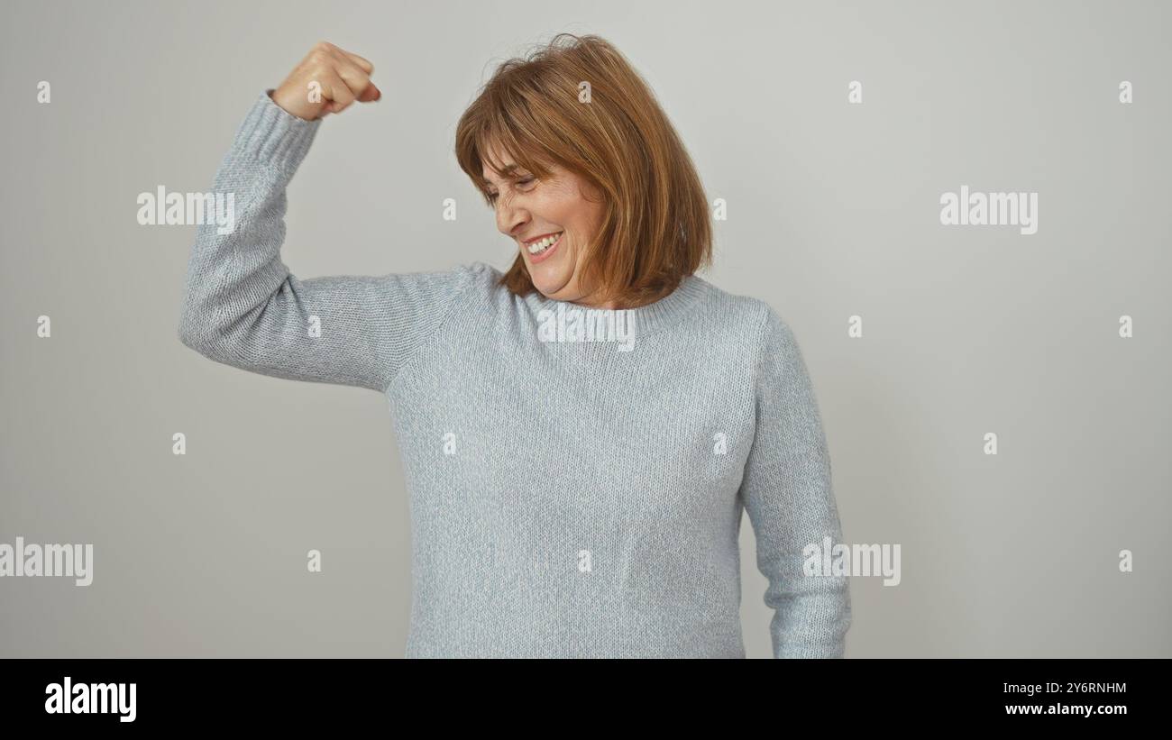 Joyful middle-aged woman flexing arm muscles against isolated white ...