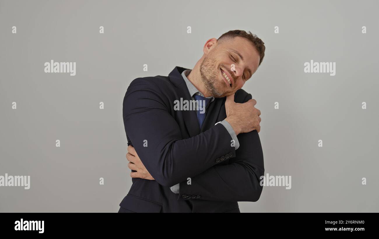 Handsome man hugging himself with a content smile in a suit against a ...