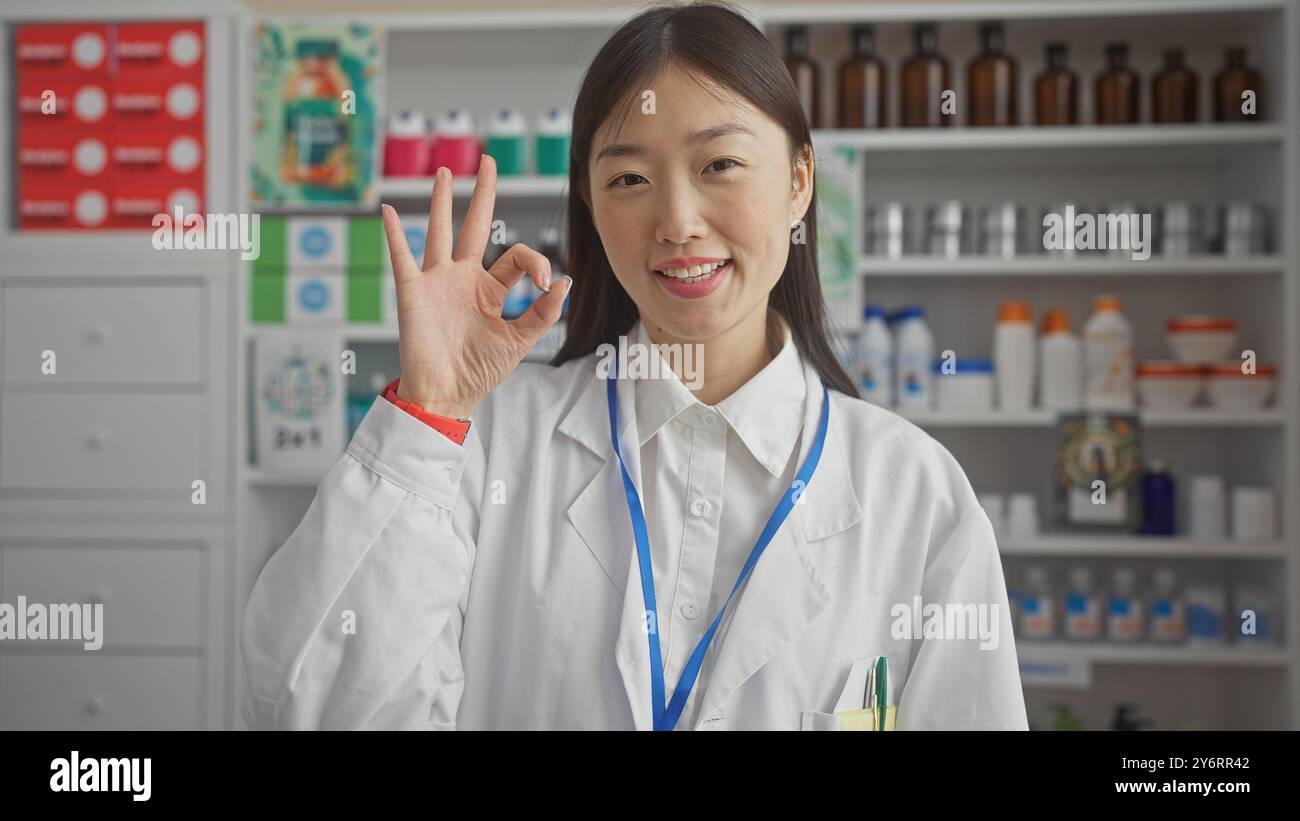 A smiling asian woman pharmacist in a drugstore gesturing okay with ...