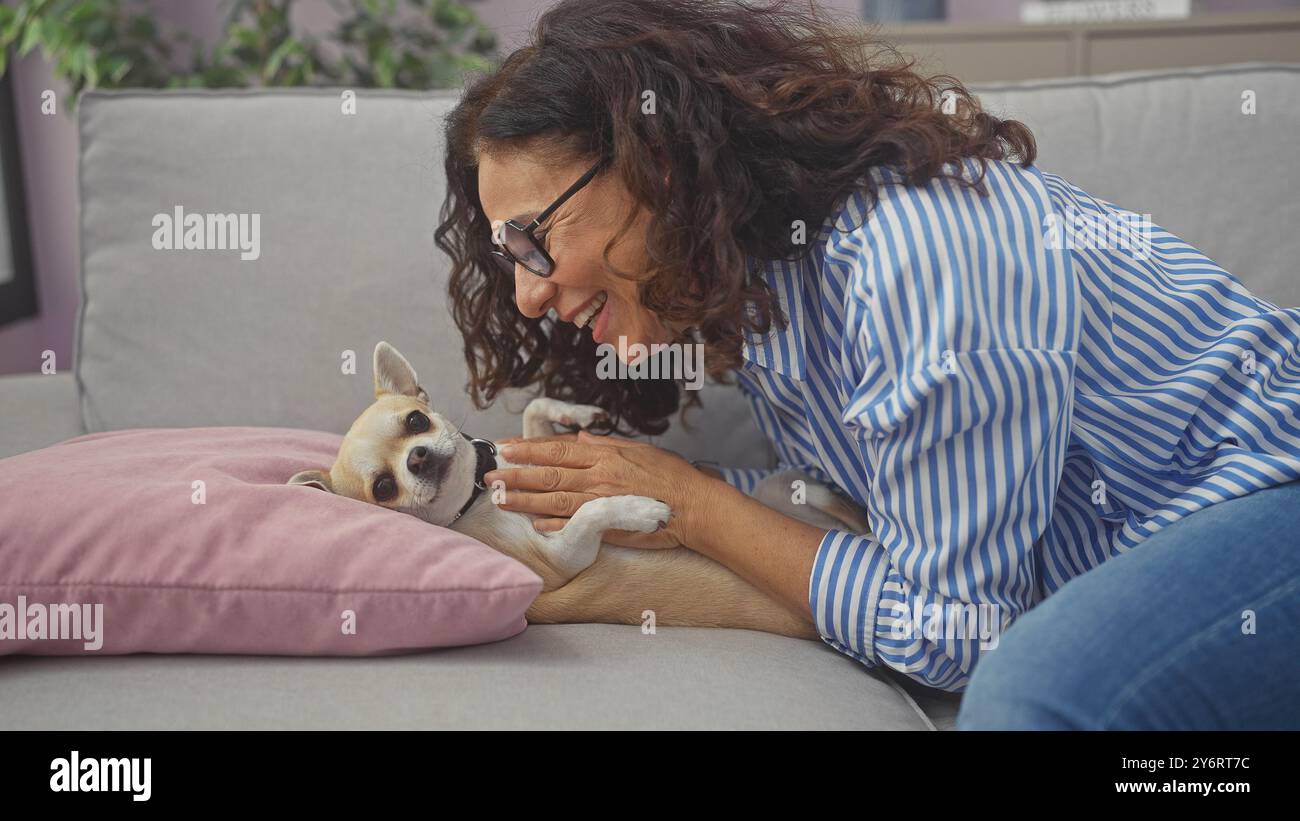 Middle-aged hispanic woman smiling at her pet chihuahua on a couch in a cozy living room Stock ...