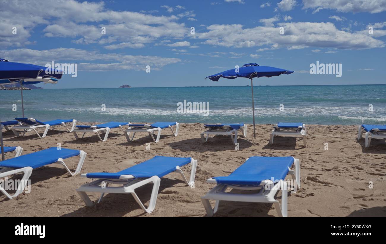 Blue sunbeds and umbrellas on a sandy beach overlooking the calm sea ...