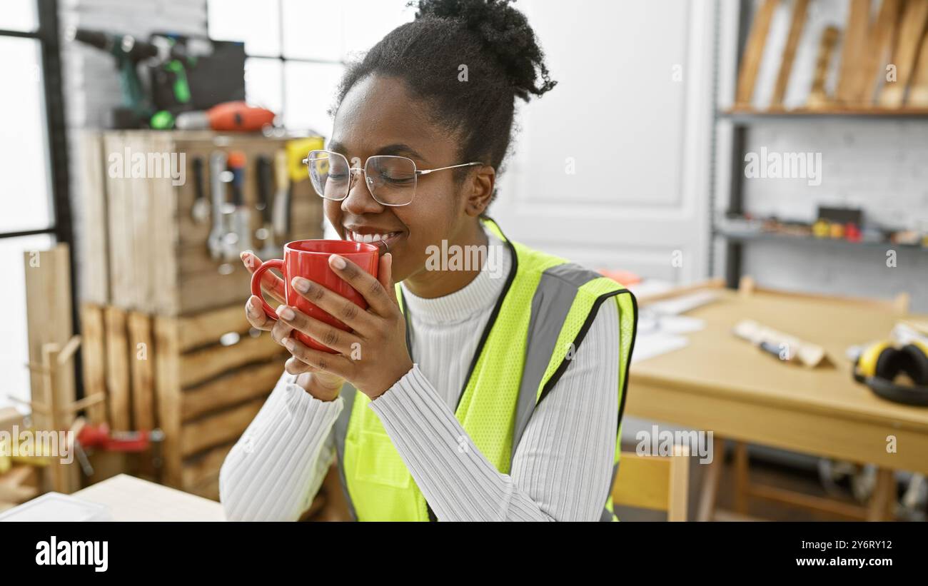 A content african woman in a reflective vest enjoys a coffee break in a ...