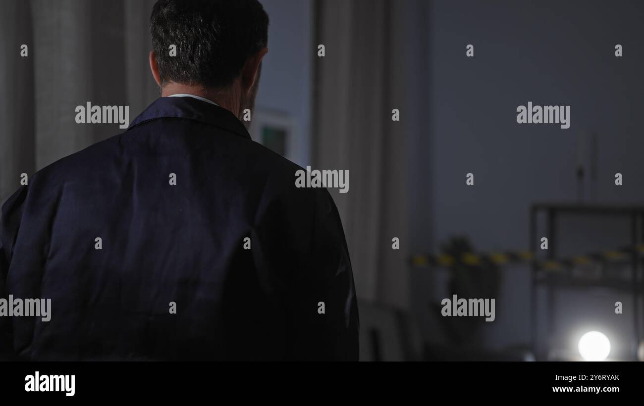 Rear view of a middle-aged man investigating a dark crime scene with ...