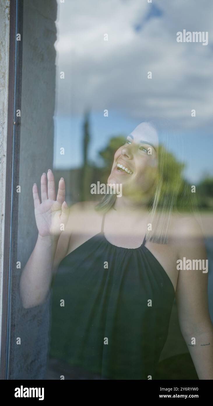 A young hispanic woman smiling indoors, her hand touching a glass ...