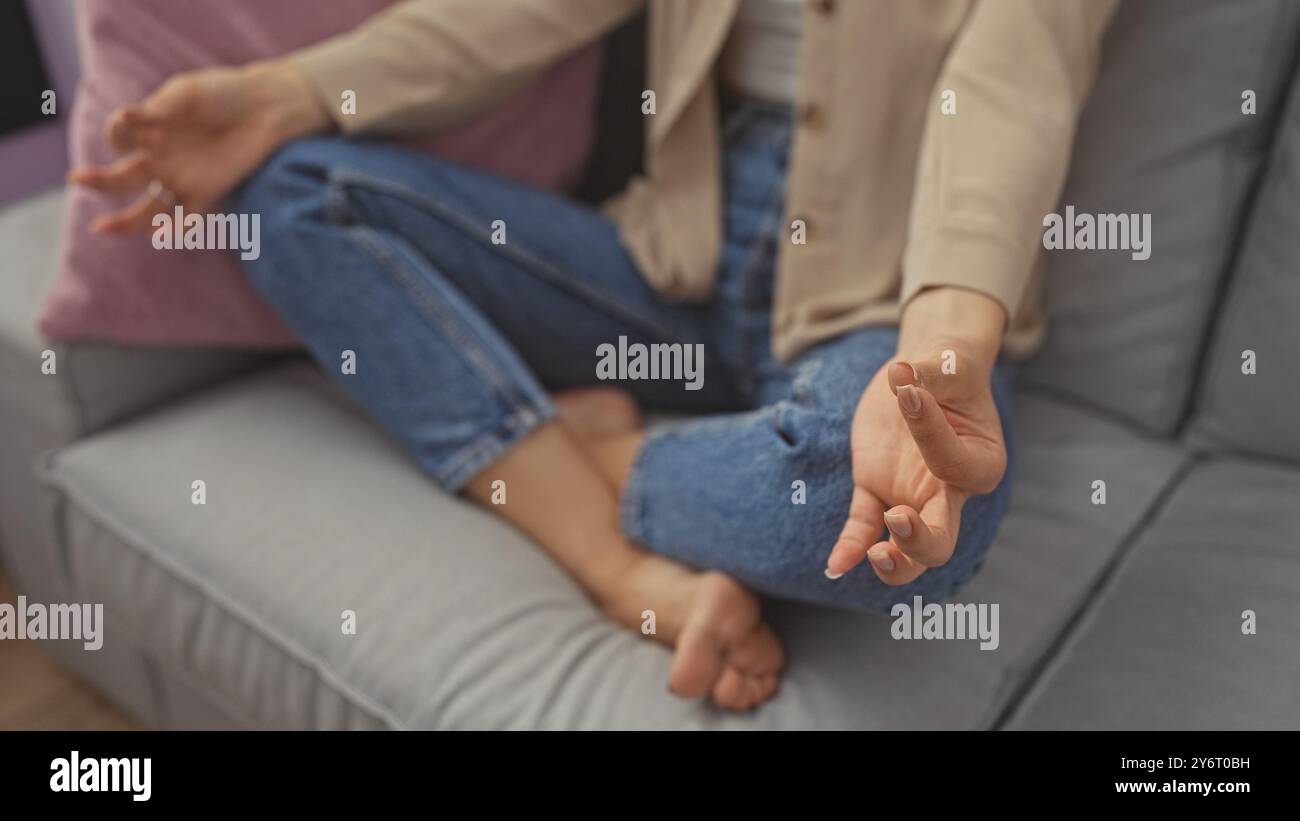 A young woman meditates in a cozy living room, sitting cross-legged on ...