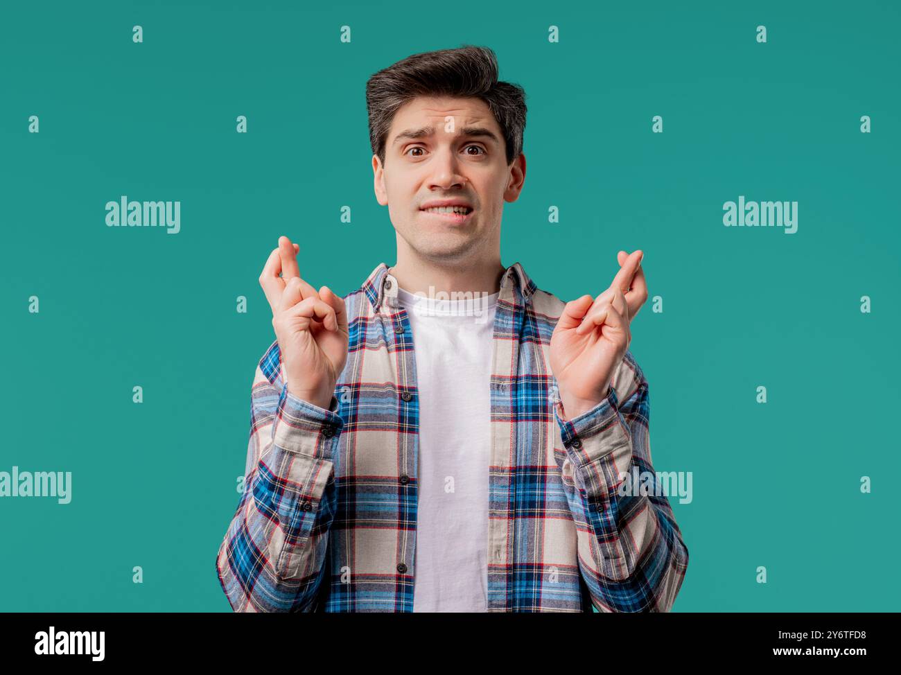 Adult 30s man praying with crossed fingers on blue background. Guy begs ...