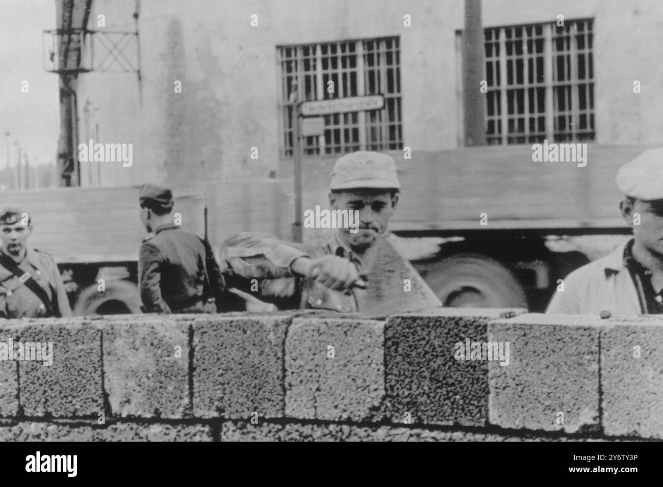 Grim faced East German construction workers under the watchful eye of ...