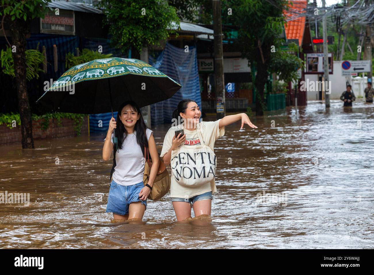 Women seen walking through a heavily flooded street on Sridonchai Road ...