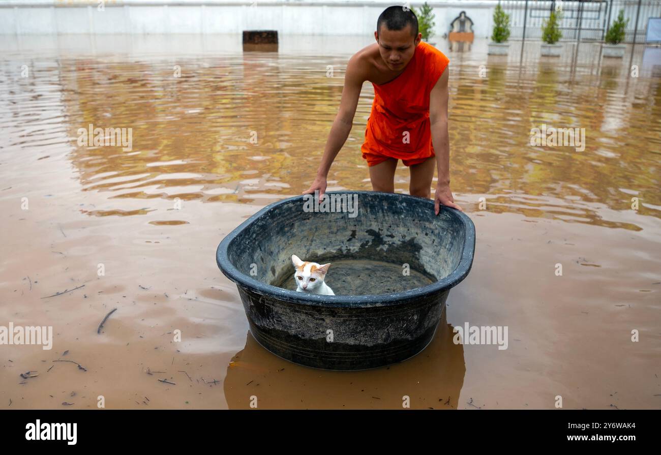 A novice monk and a cat in a basin seen walking inside a flooded temple ...