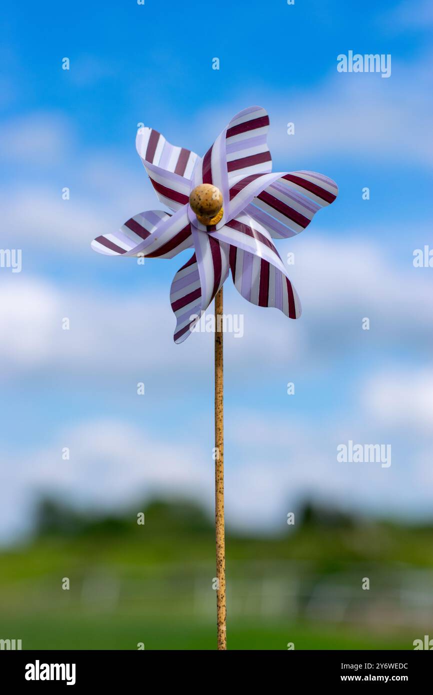 A colorful pinwheel with red and white stripes stands against a blurred ...