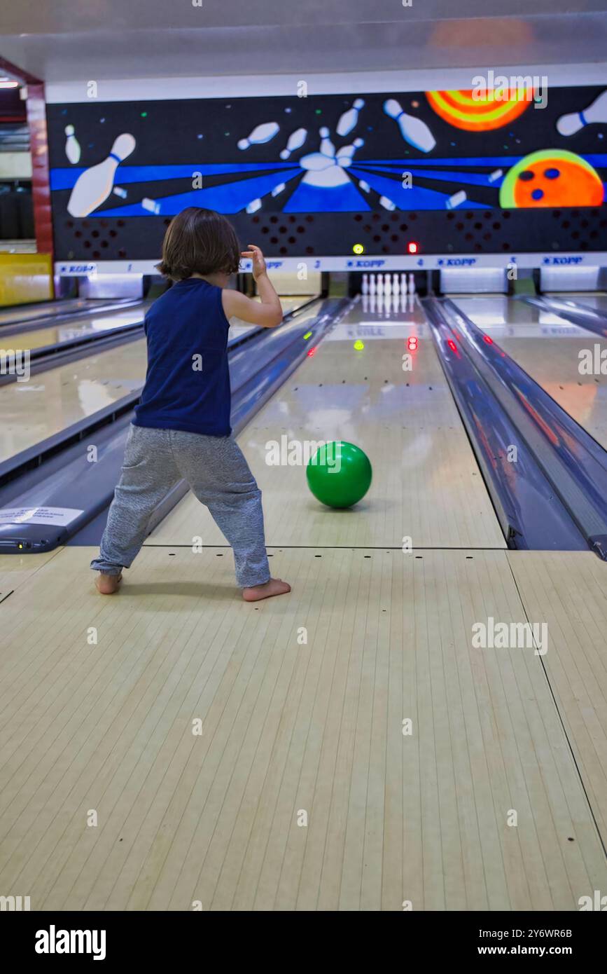 A young boy is bowling with a green ball. The bowling alley is ...