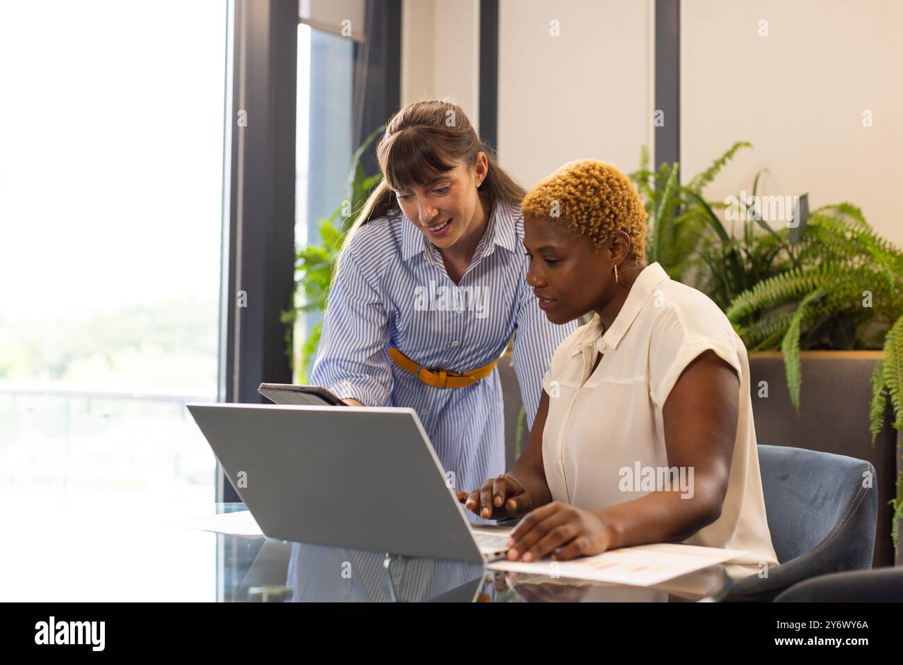 Collaborating on project, two women using laptop and tablet in modern ...