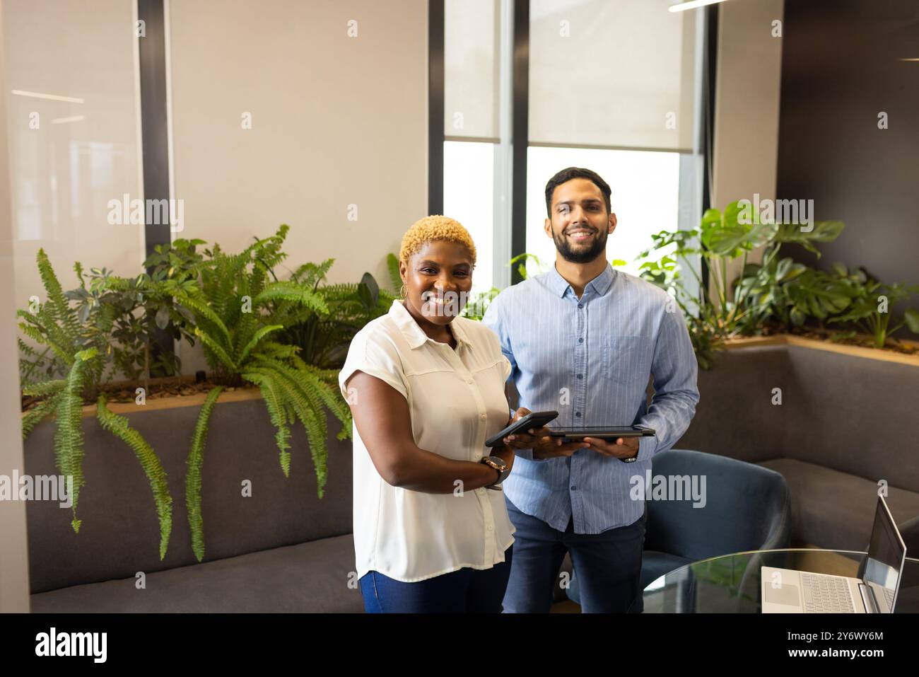 Smiling colleagues holding tablets in modern office with indoor plants ...
