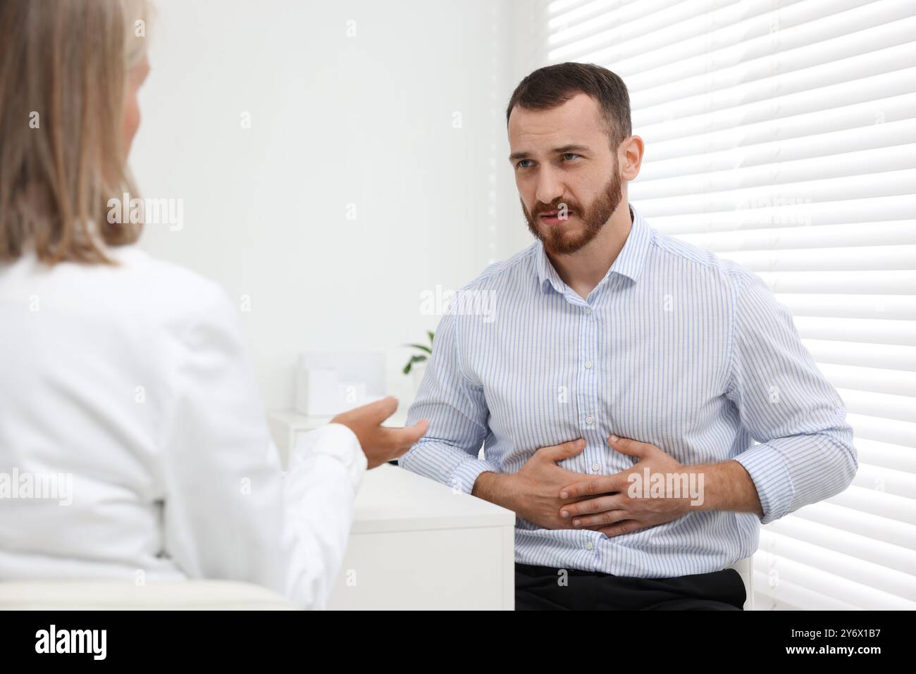 Doctor consulting patient with stomach pain at table in clinic, back ...