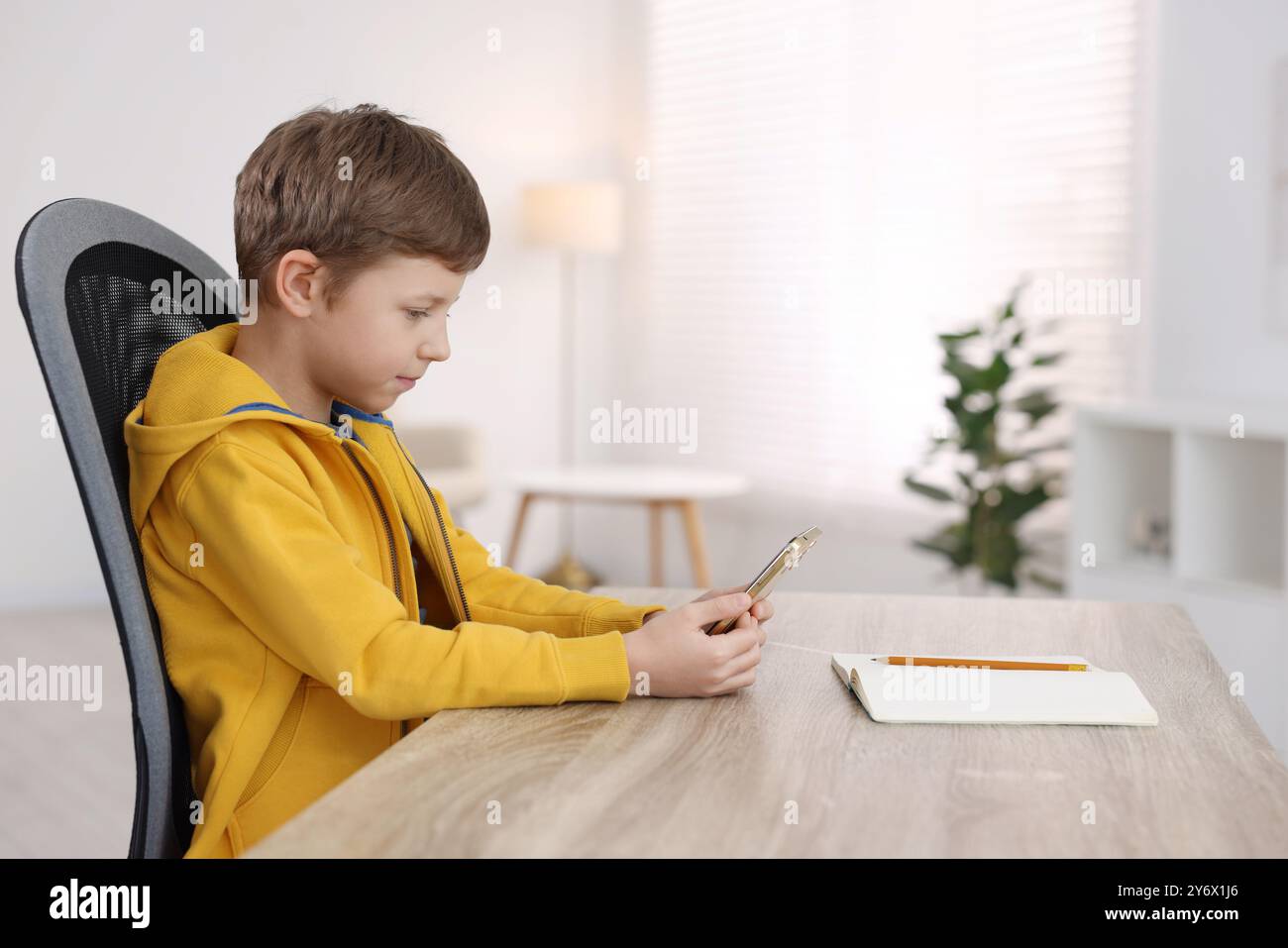 Boy with correct posture using smartphone at wooden desk indoors Stock ...