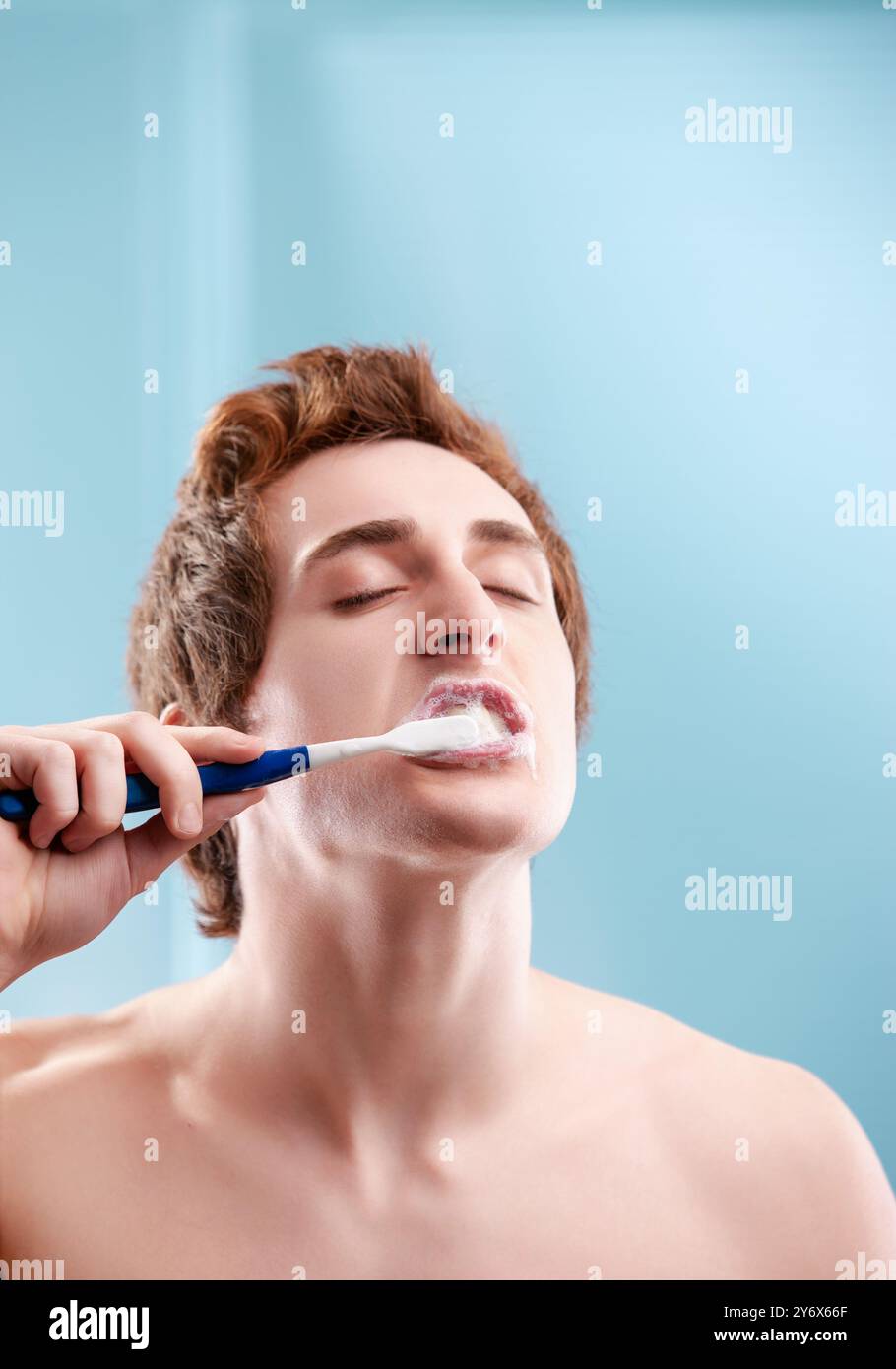 Young man with eyes closed is carefully brushing his teeth in the ...