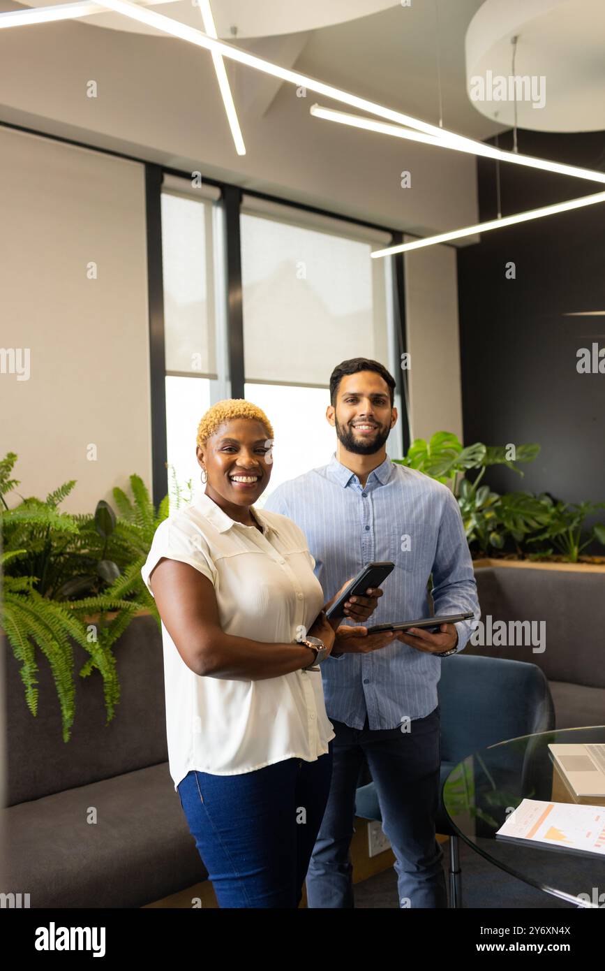 Smiling colleagues holding tablets and collaborating in modern office ...