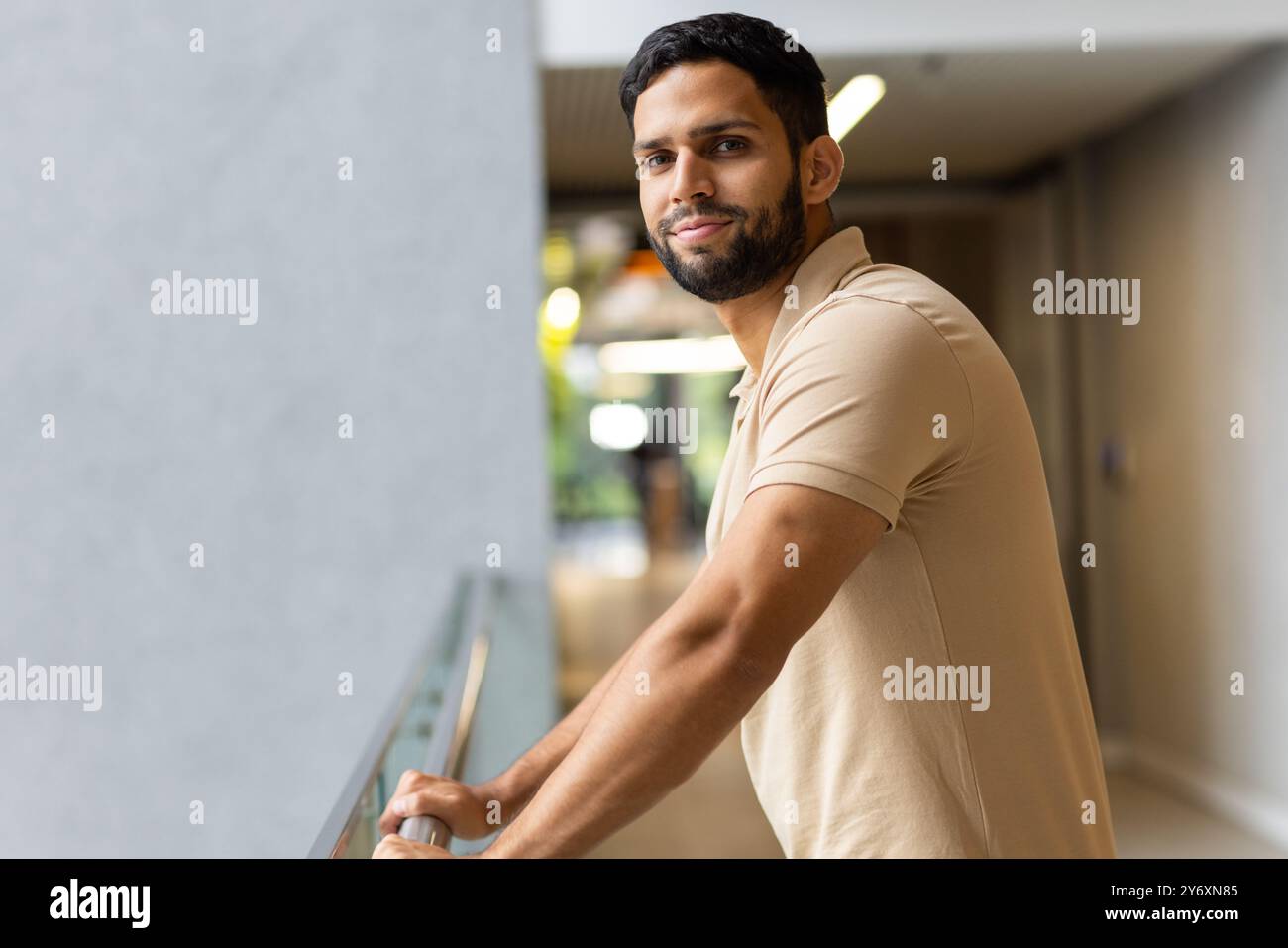 Smiling man leaning on railing in modern office hallway, looking ...