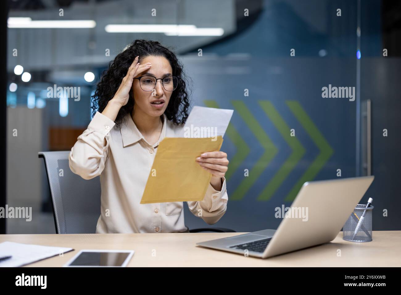 Businesswoman expressing shock while reading letter on desk next to ...
