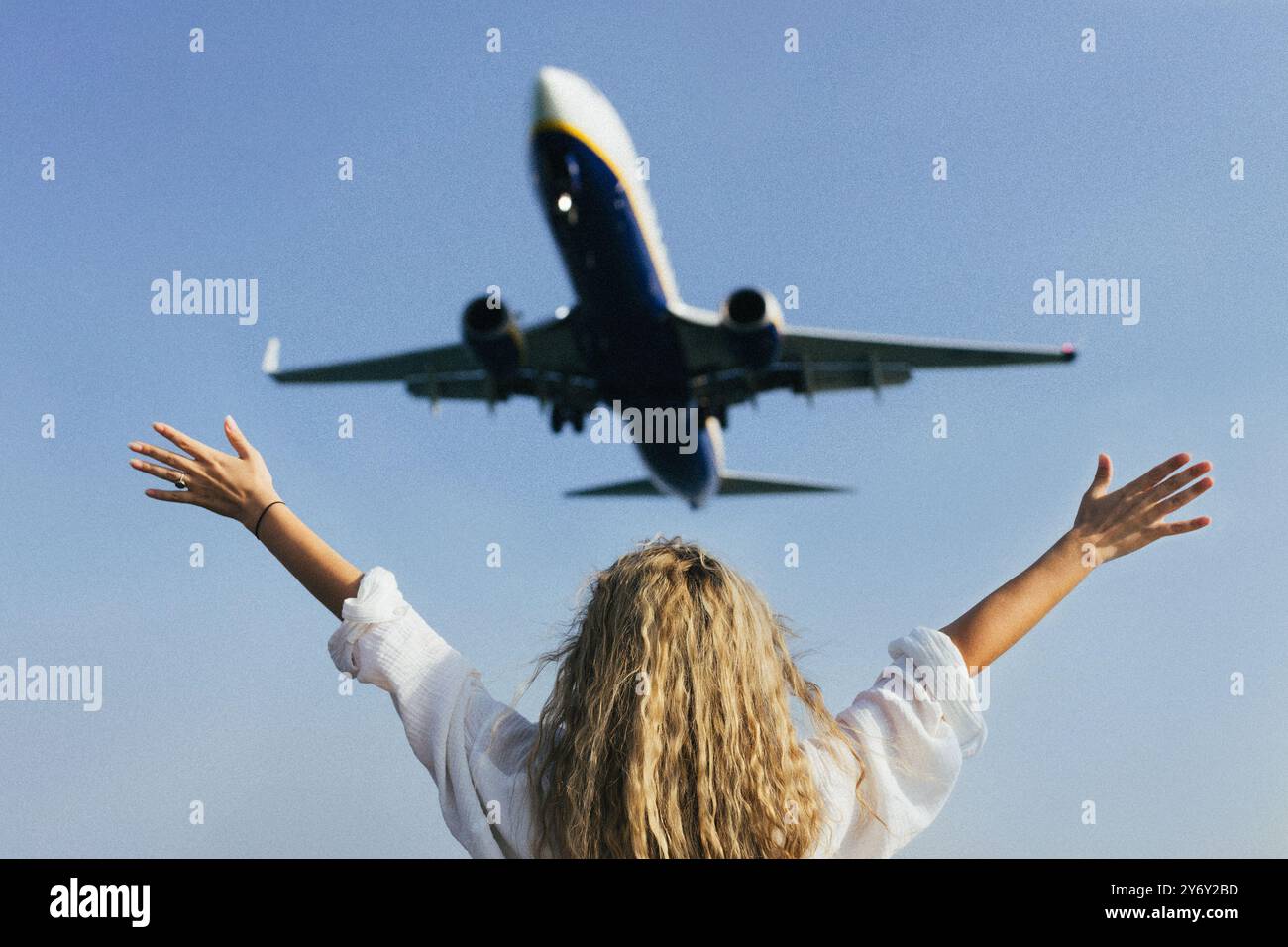 A woman with her arms raised above her head waves at an airplane flying ...