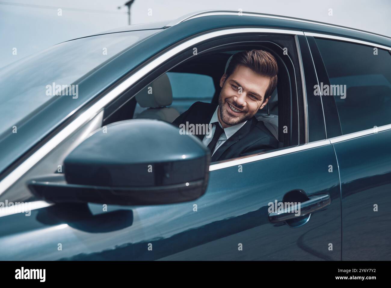 Happy driver. Handsome young man in full suit looking straight while ...