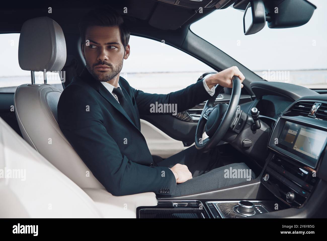 Busy driver. Handsome young man in full suit looking over shoulder ...