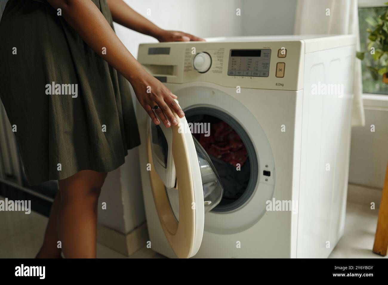 Person loading clothes into washing machine in modern home laundry room ...
