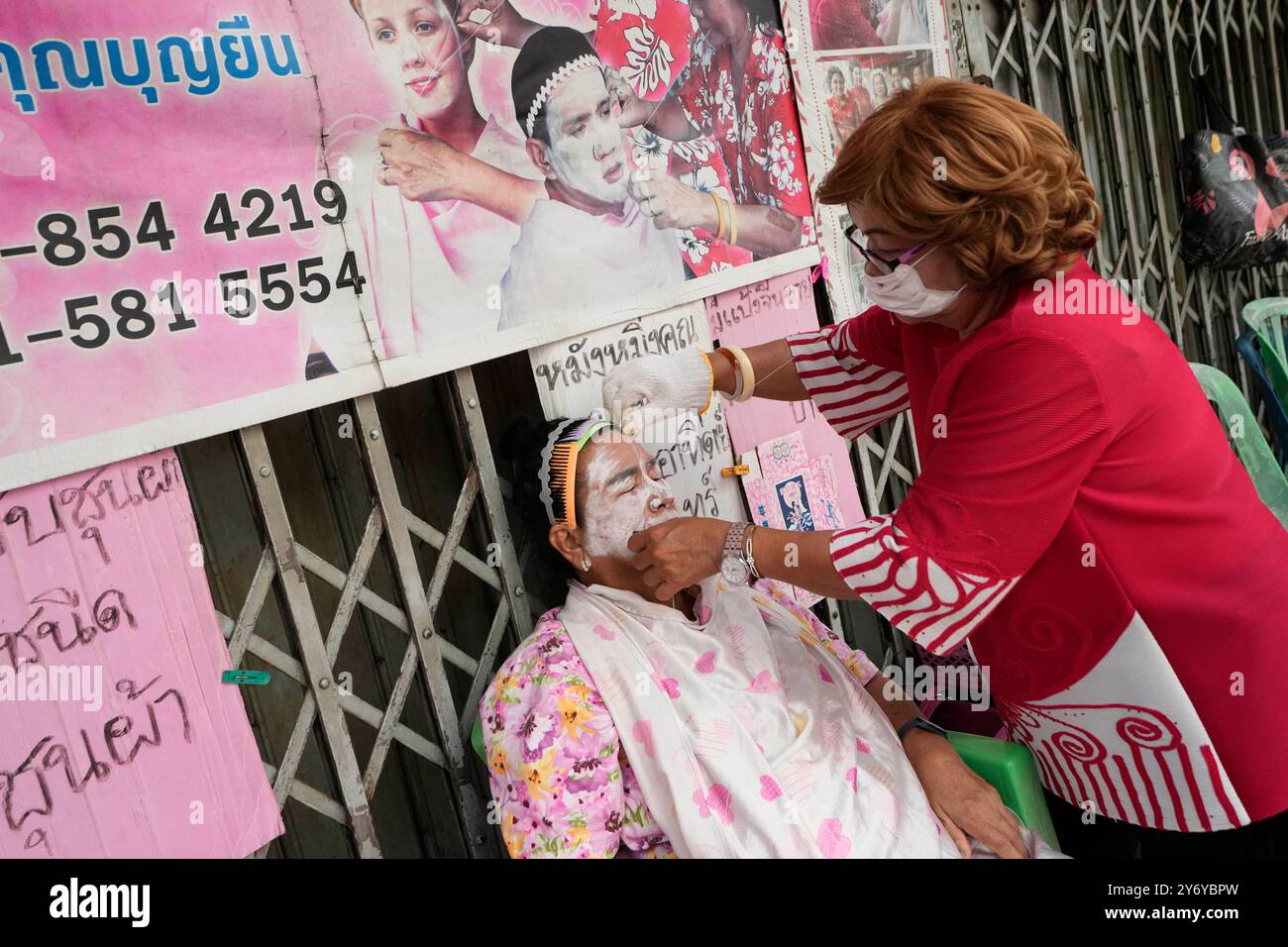 A roadside beautician uses a threading technique to remove hair for a ...