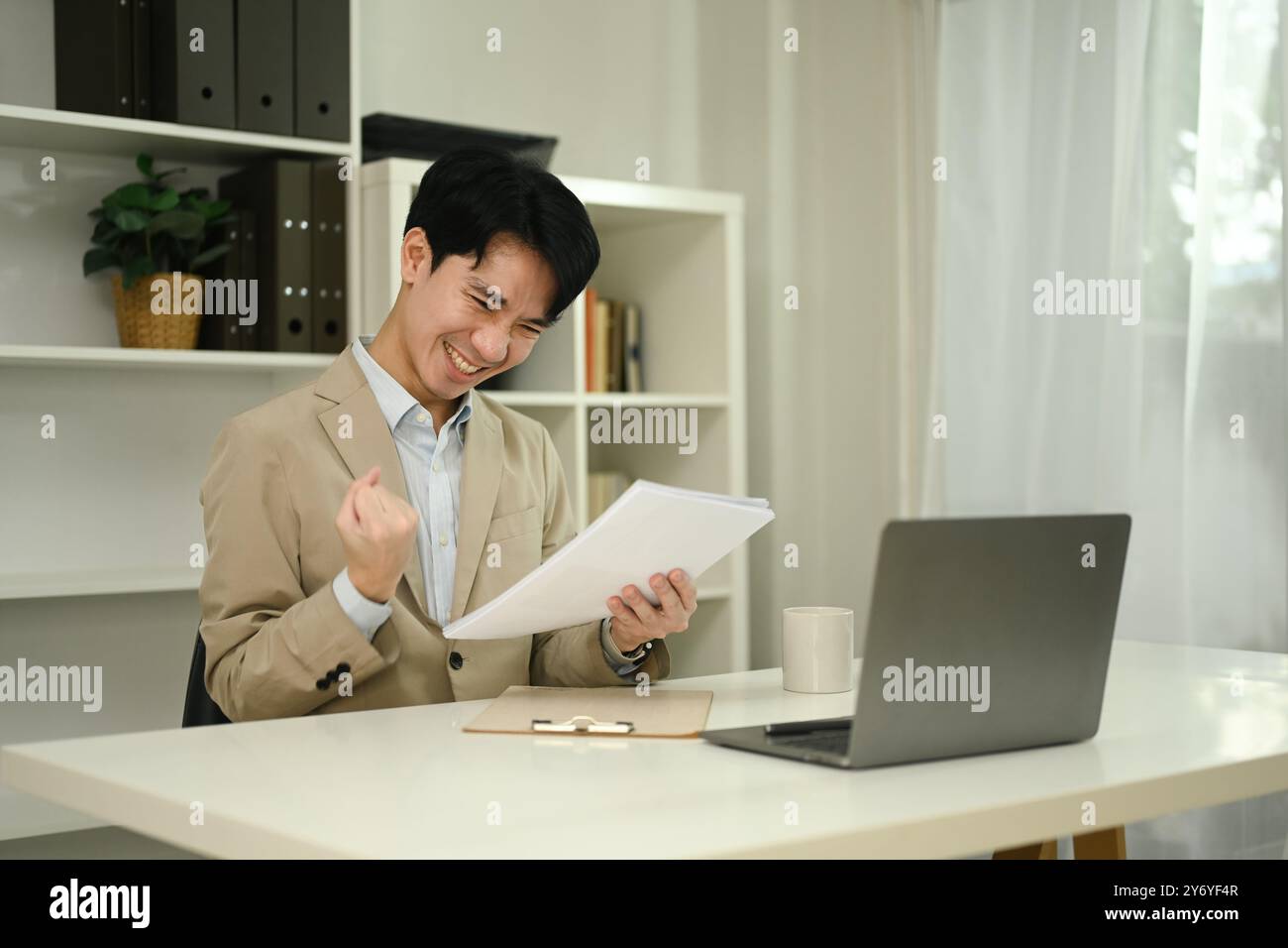 Overwhelmed businessman holding a document, raising hand in yes gesture ...