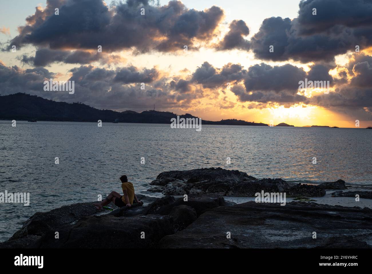One man, sitted on the rocks, during a golden sunset at beach Stock ...