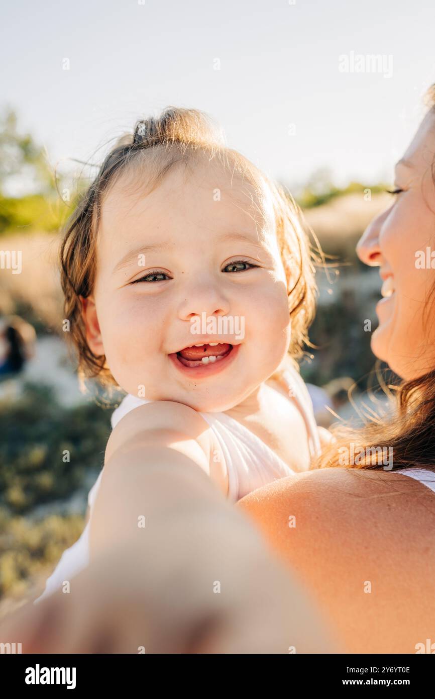Smiling baby reaching towards camera, held by mother Stock Photo - Alamy