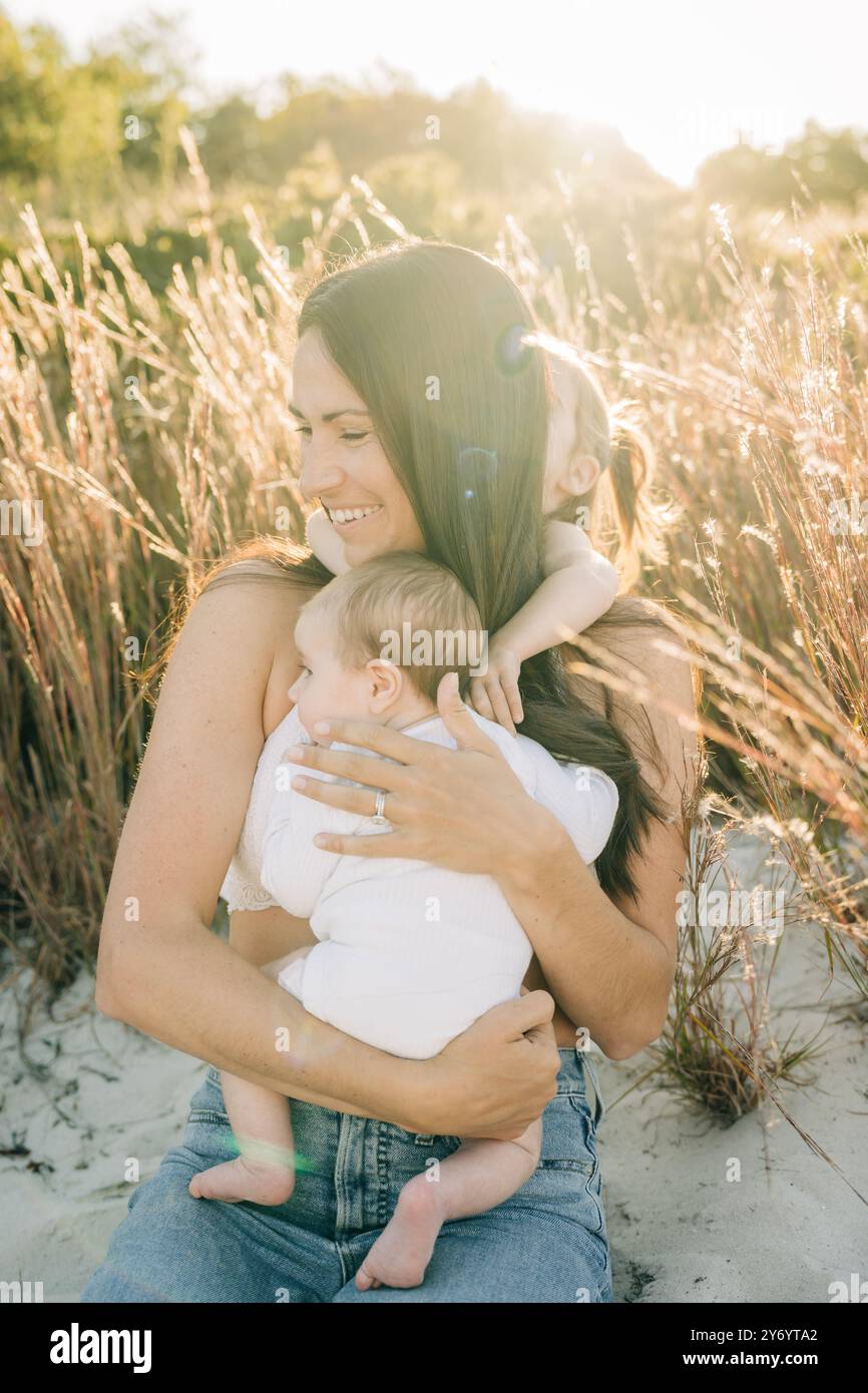 Mother holding baby with toddler hugging her from behind Stock Photo ...