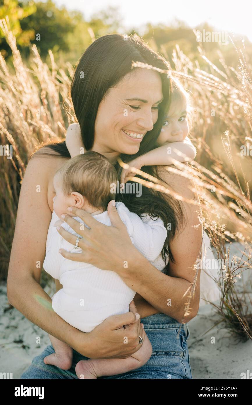 Mother holding baby with toddler hugging her from behind Stock Photo ...