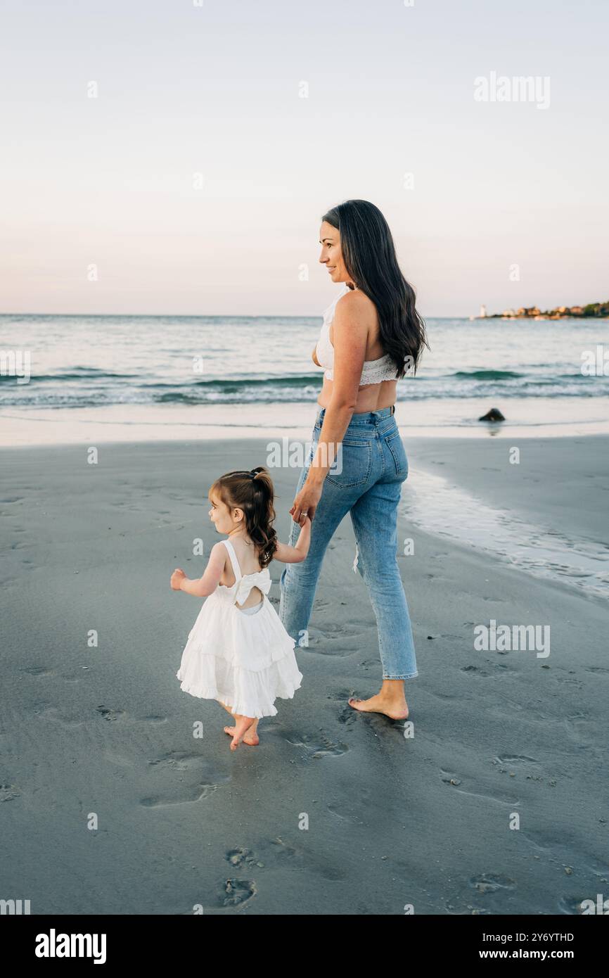 Mother and daughter holding hands, walking barefoot along the beach ...
