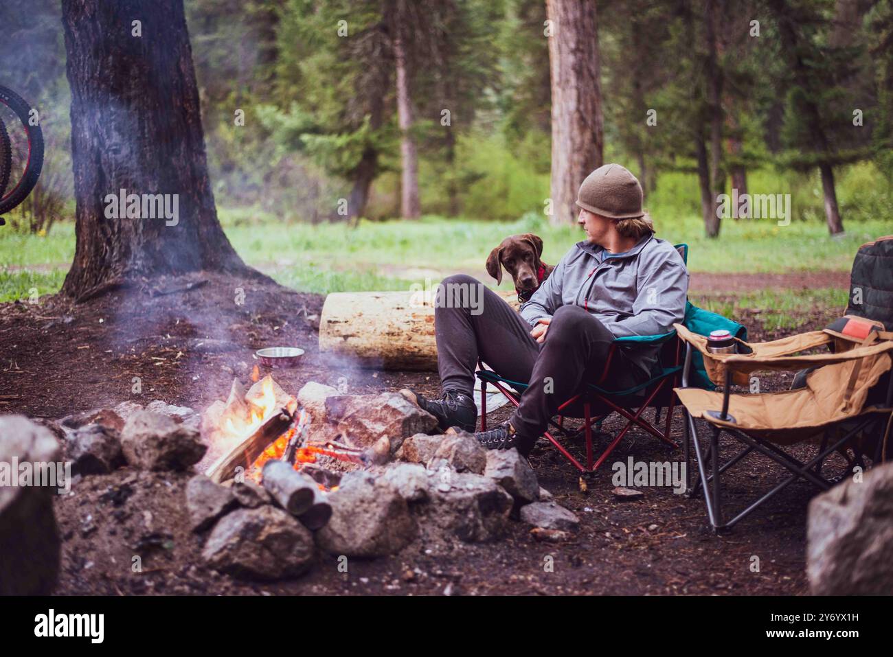 Man sitting around a campfire with dog Stock Photo - Alamy