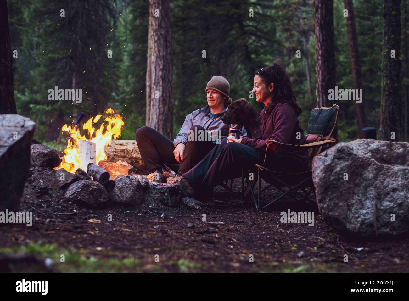 Young Couple sitting around a campfire with dog in a dark forest Stock ...