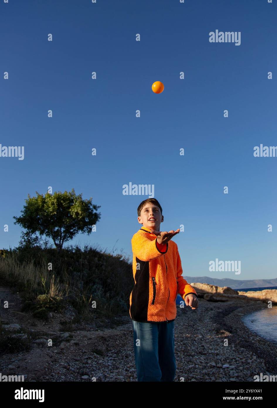 Boy is throws up orange color small ball outdoors Stock Photo - Alamy