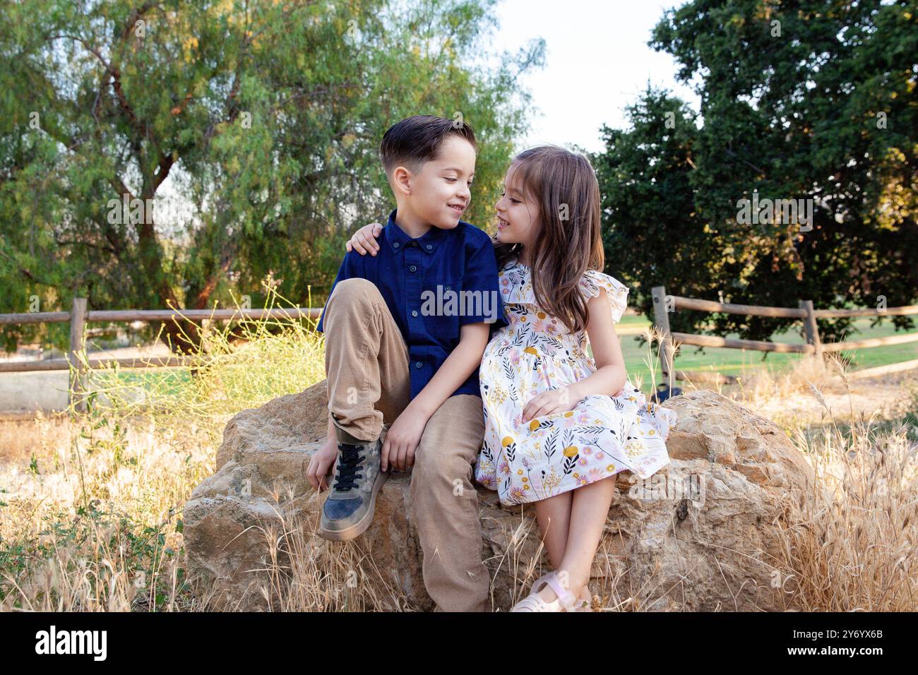A young boy and girl sitting on a rock outdoors, smiling Stock Photo ...