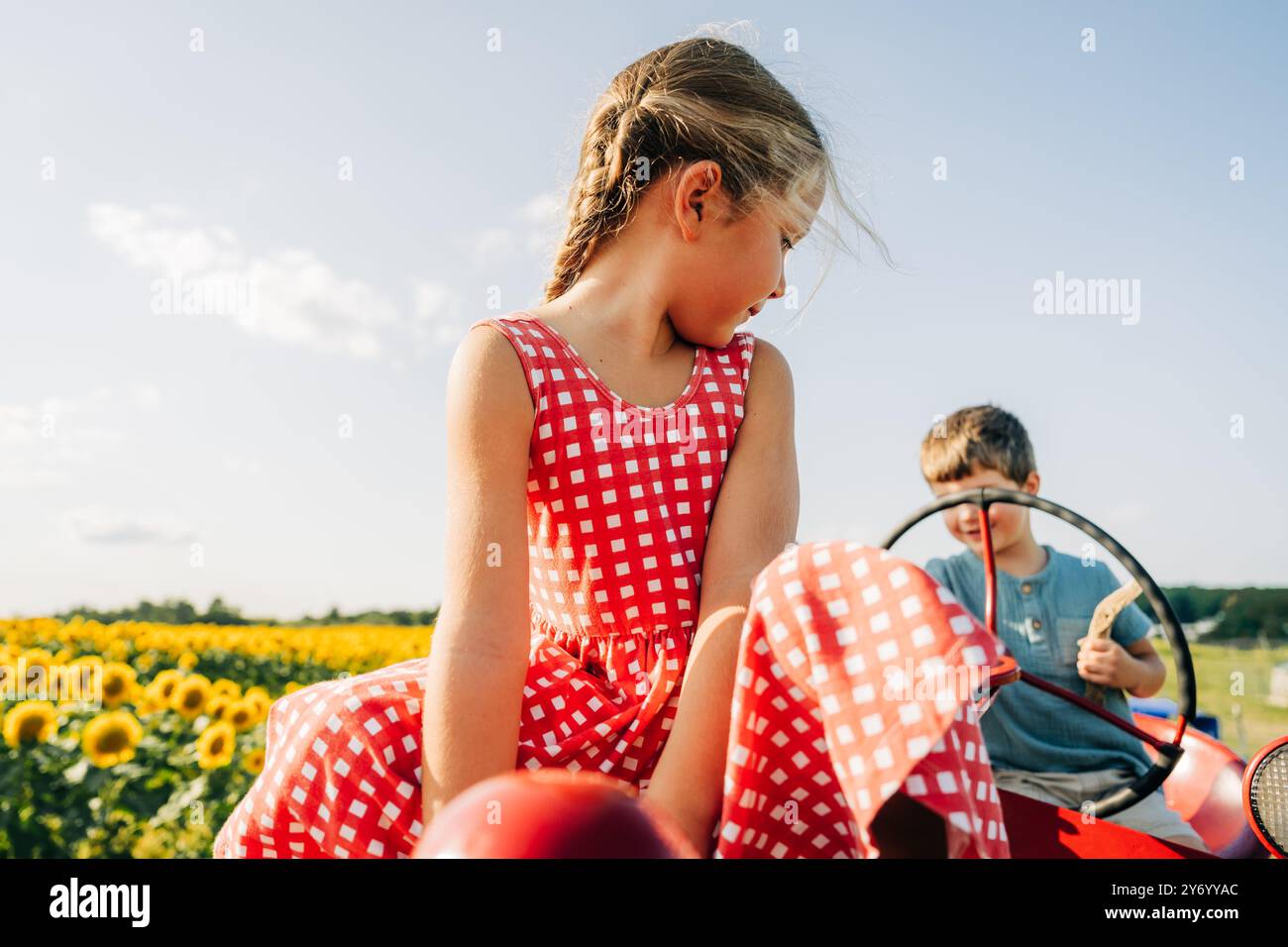A girl in a red checkered dress sitting on a tractor Stock Photo - Alamy
