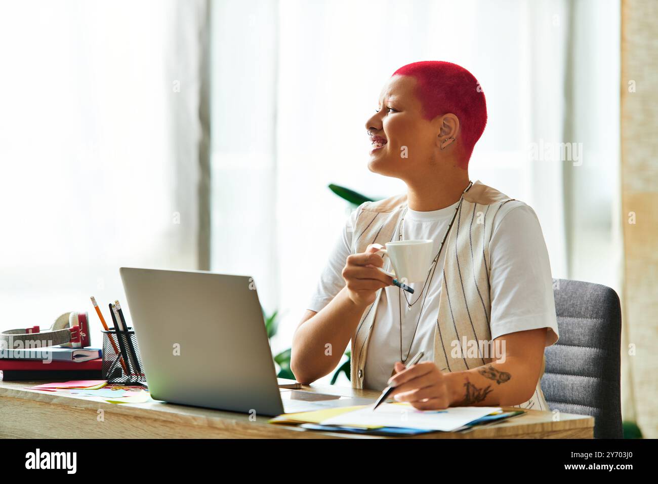 A cheerful young woman sips coffee at her desk, immersed in her ...